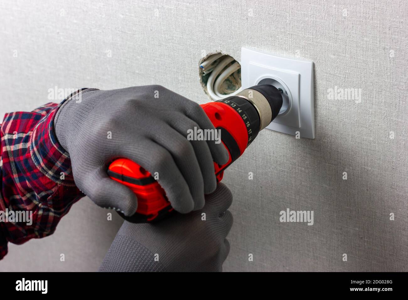 A worker, using an electric screwdriver, installs an electrical outlet ...