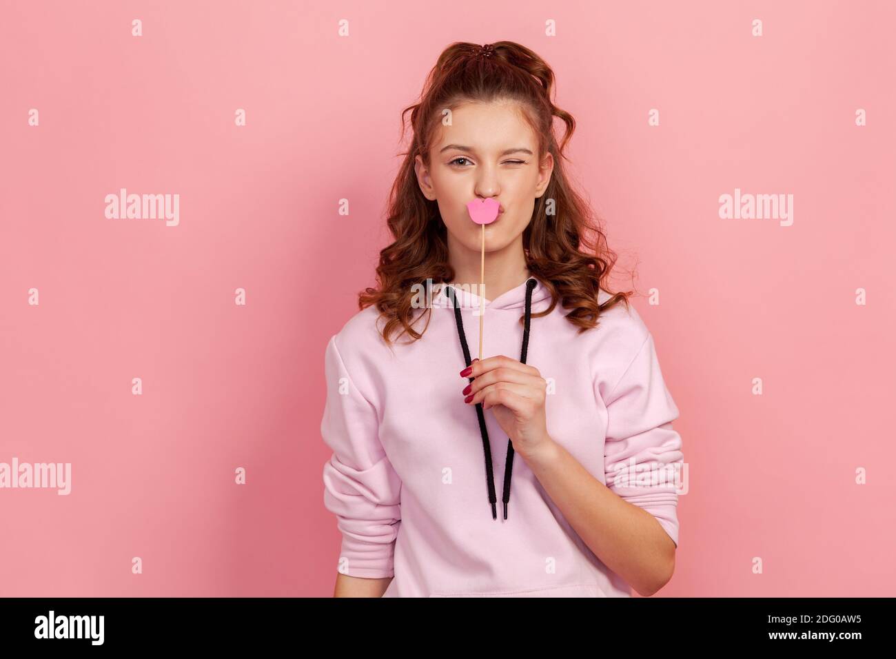 Portrait of playful young female with ponytail and hoodie holding paper ...