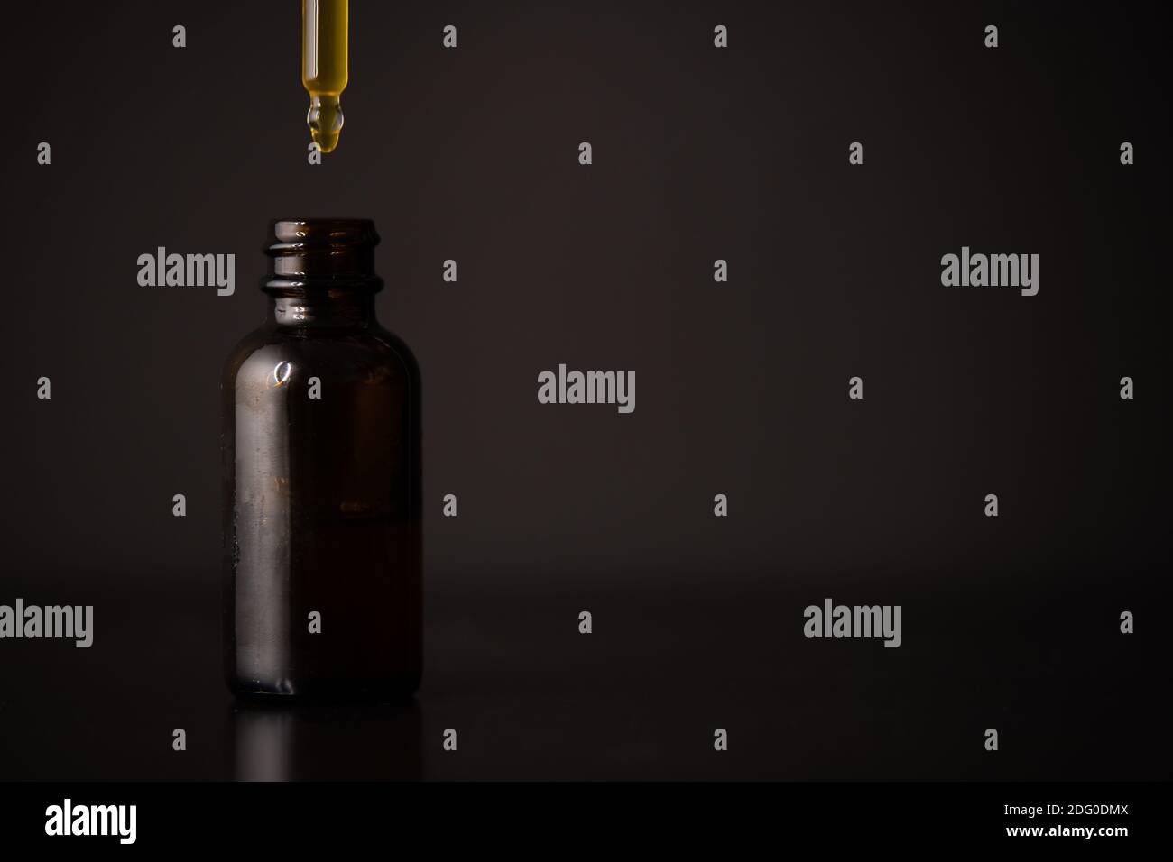 brown glass bottle with yellow dropper dripping liquid on soft black ...