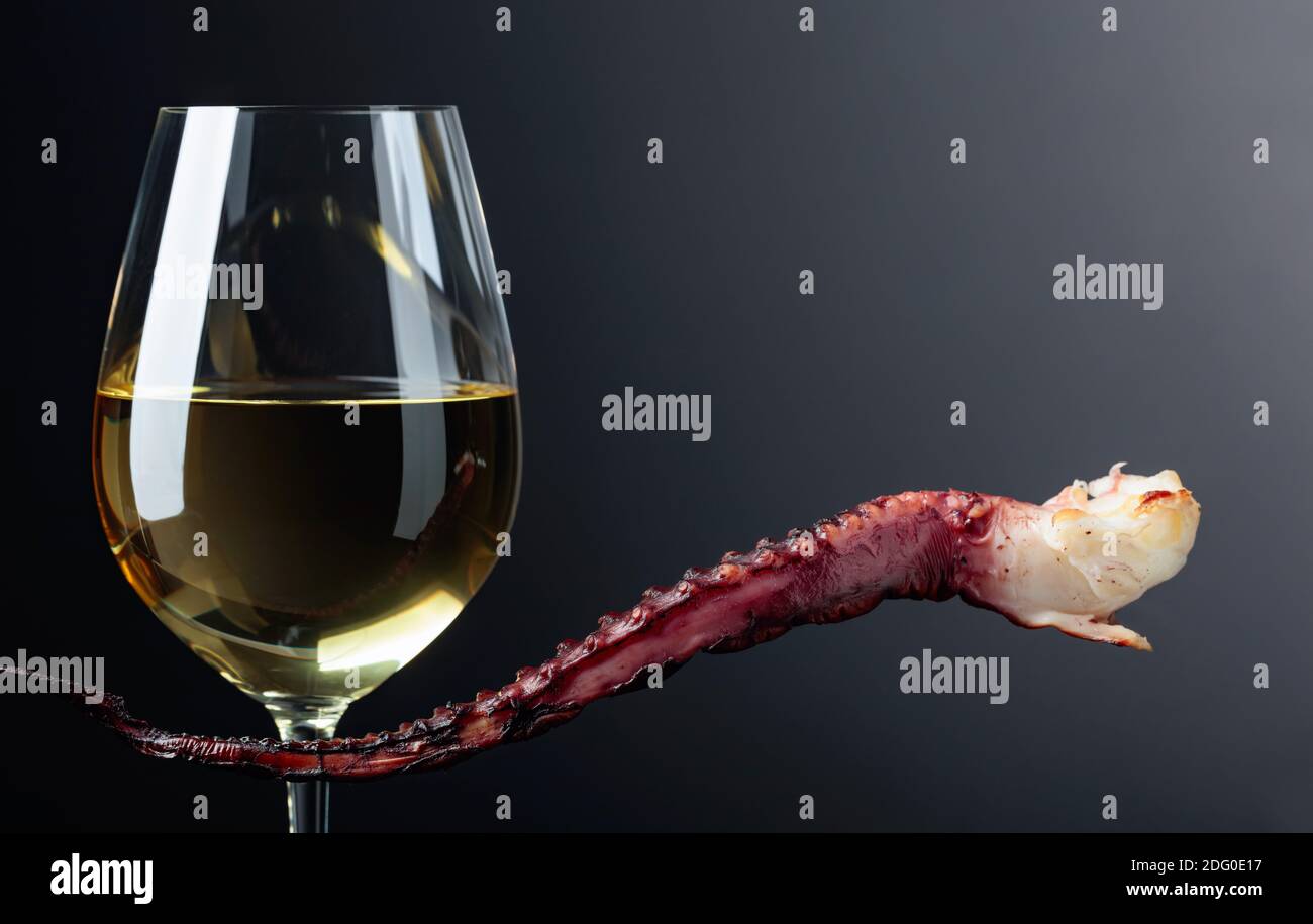 Grilled octopus and white wine glass on a black background. Copy space ...