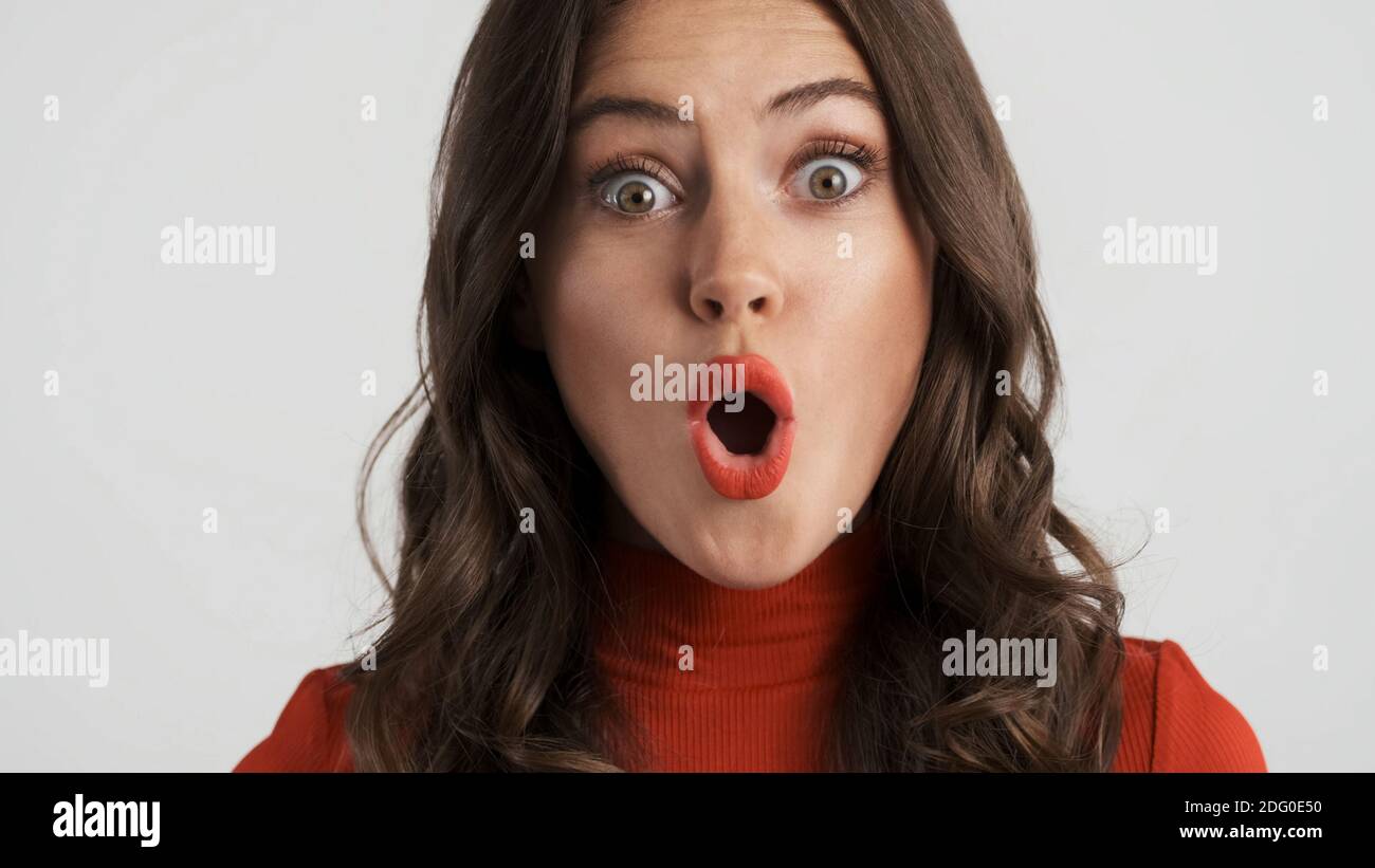Portrait of beautiful excited girl amazedly looking in camera over gray ...
