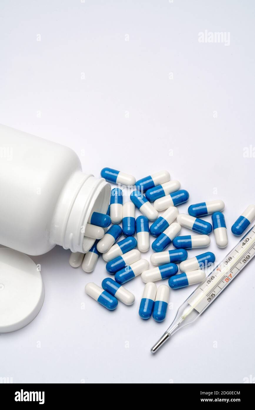 Medications capsules in a bottle and thermometer on light grey ...