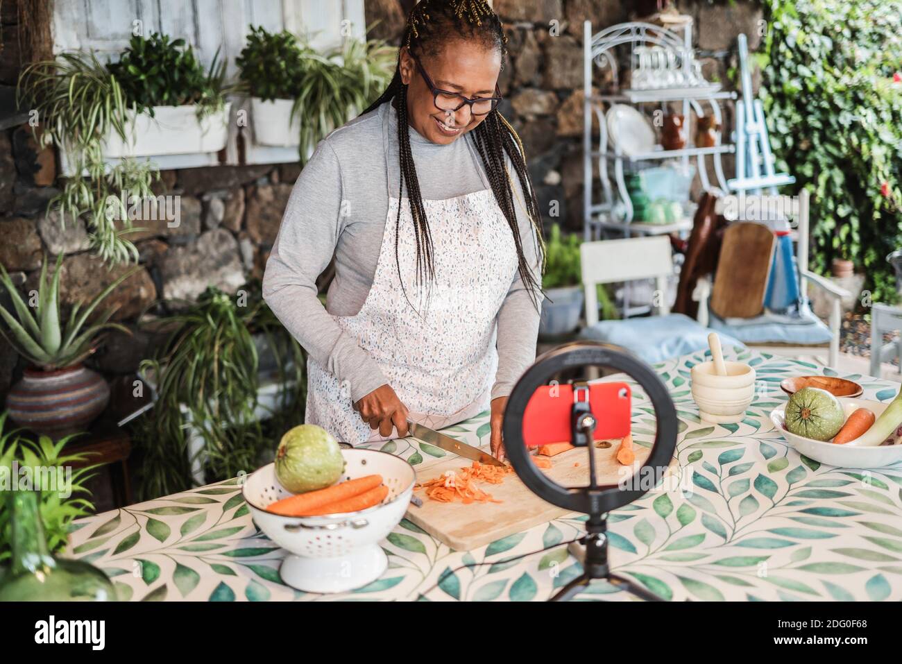 African senior woman cooking outdoor while streaming online for webinar ...