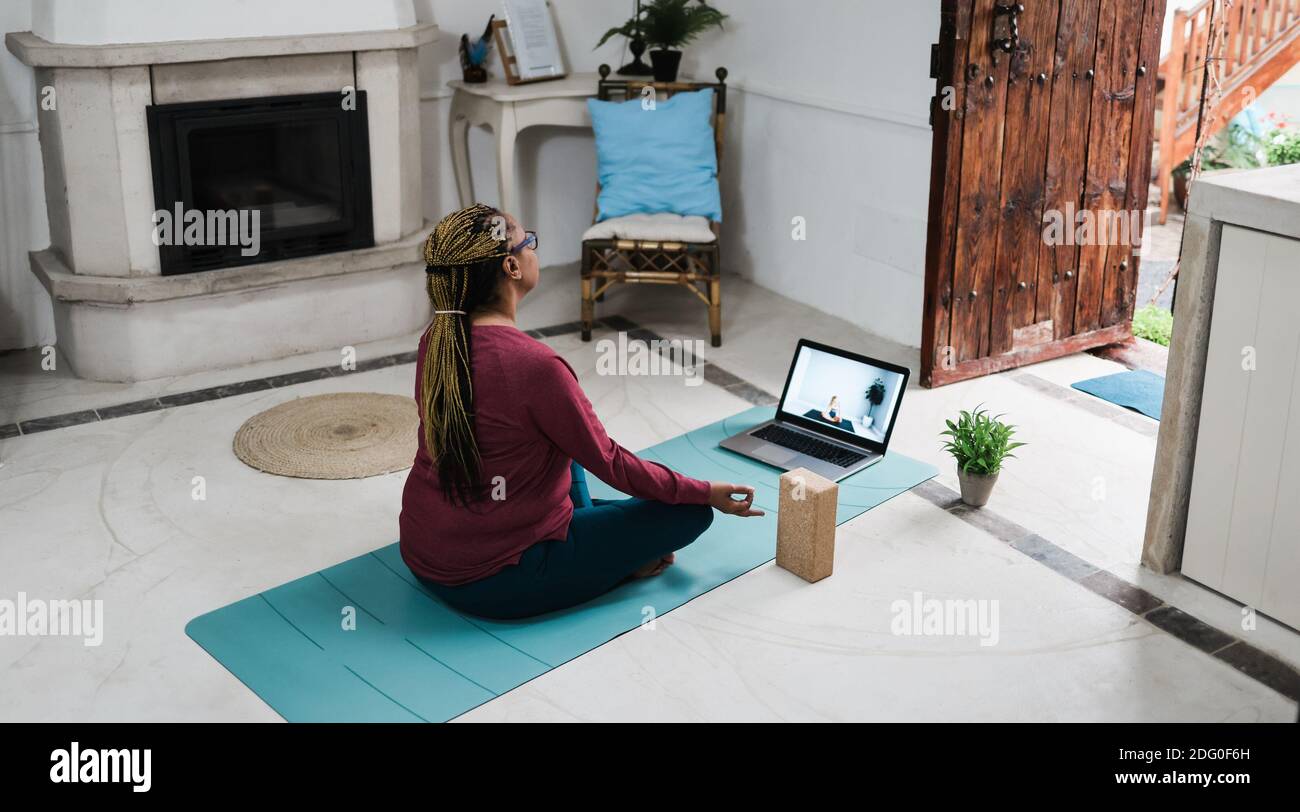 African senior woman doing online yoga lesson at home during ...