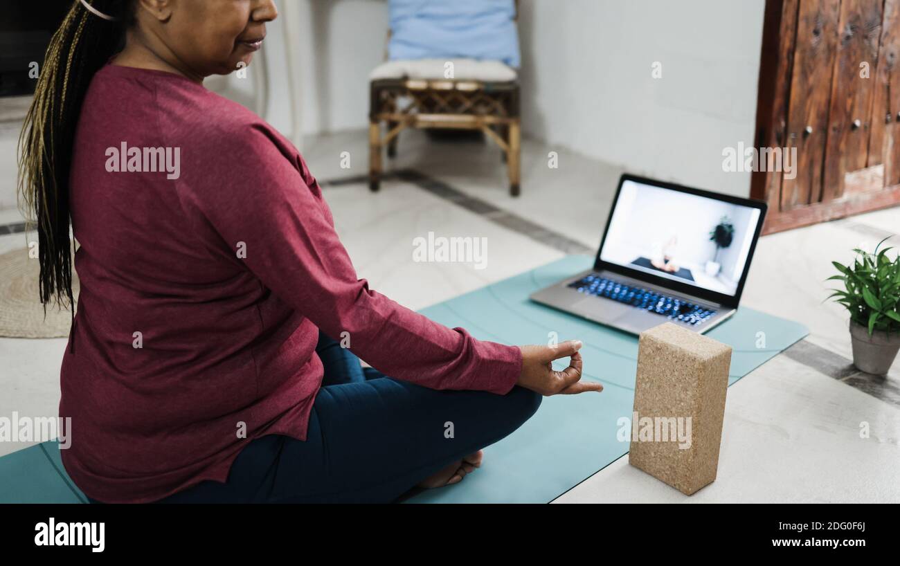African senior woman doing online yoga lesson at home during ...