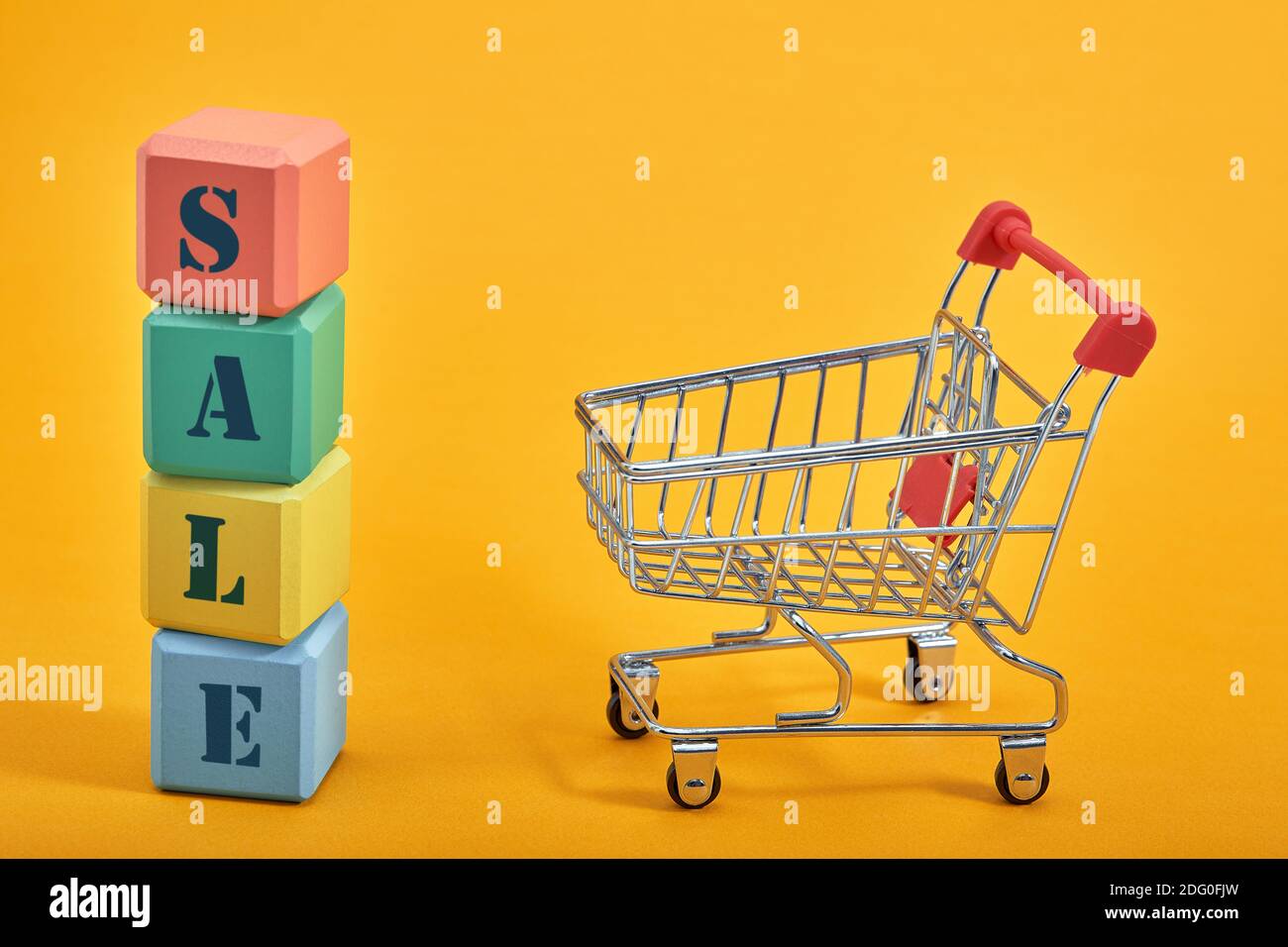 A miniature shopping cart and multi-colored cubes on yellow background ...