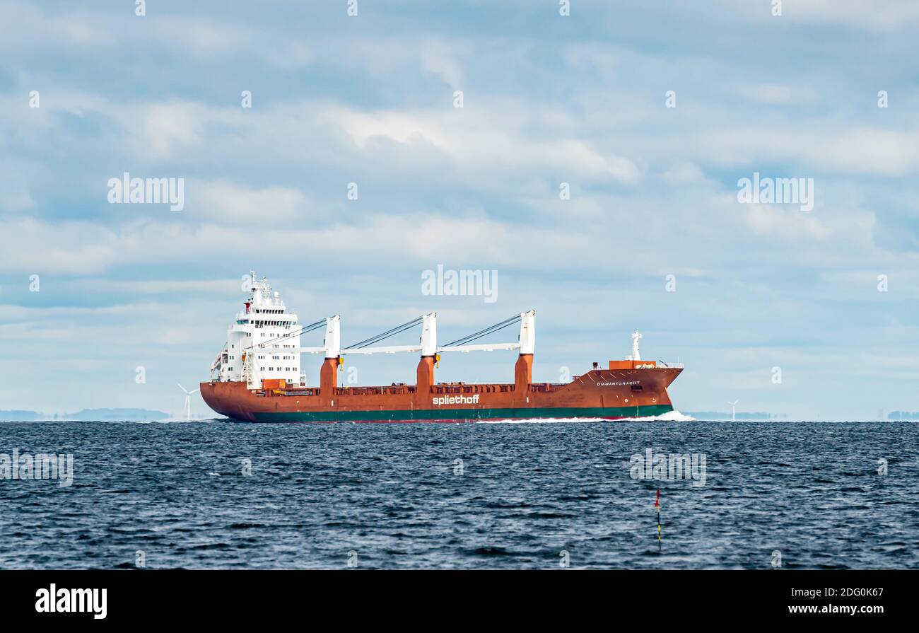 Red cargo ship with large cranes mounted onboard, sailing out to sea ...