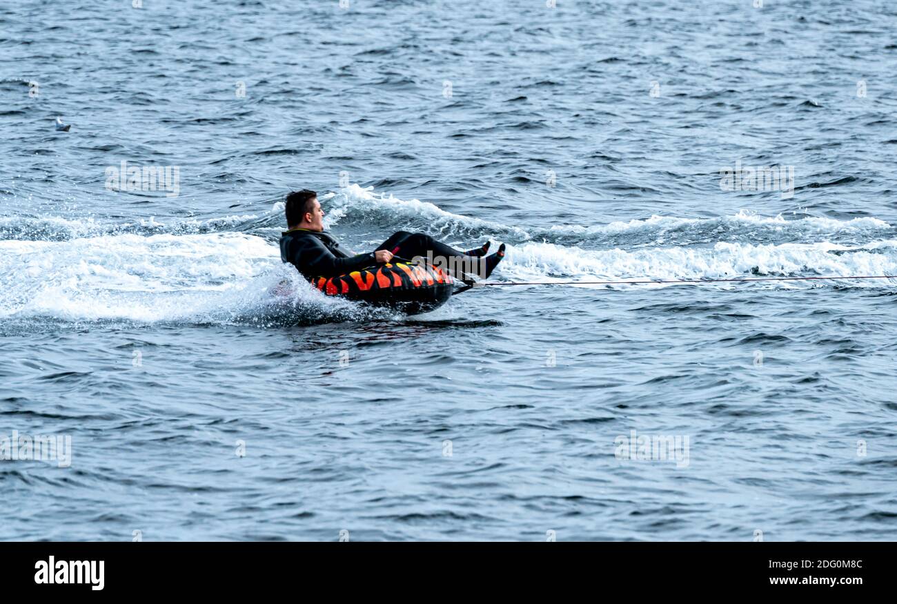 Man on an inflatable ring getting towed behind a jet ski near the beach ...