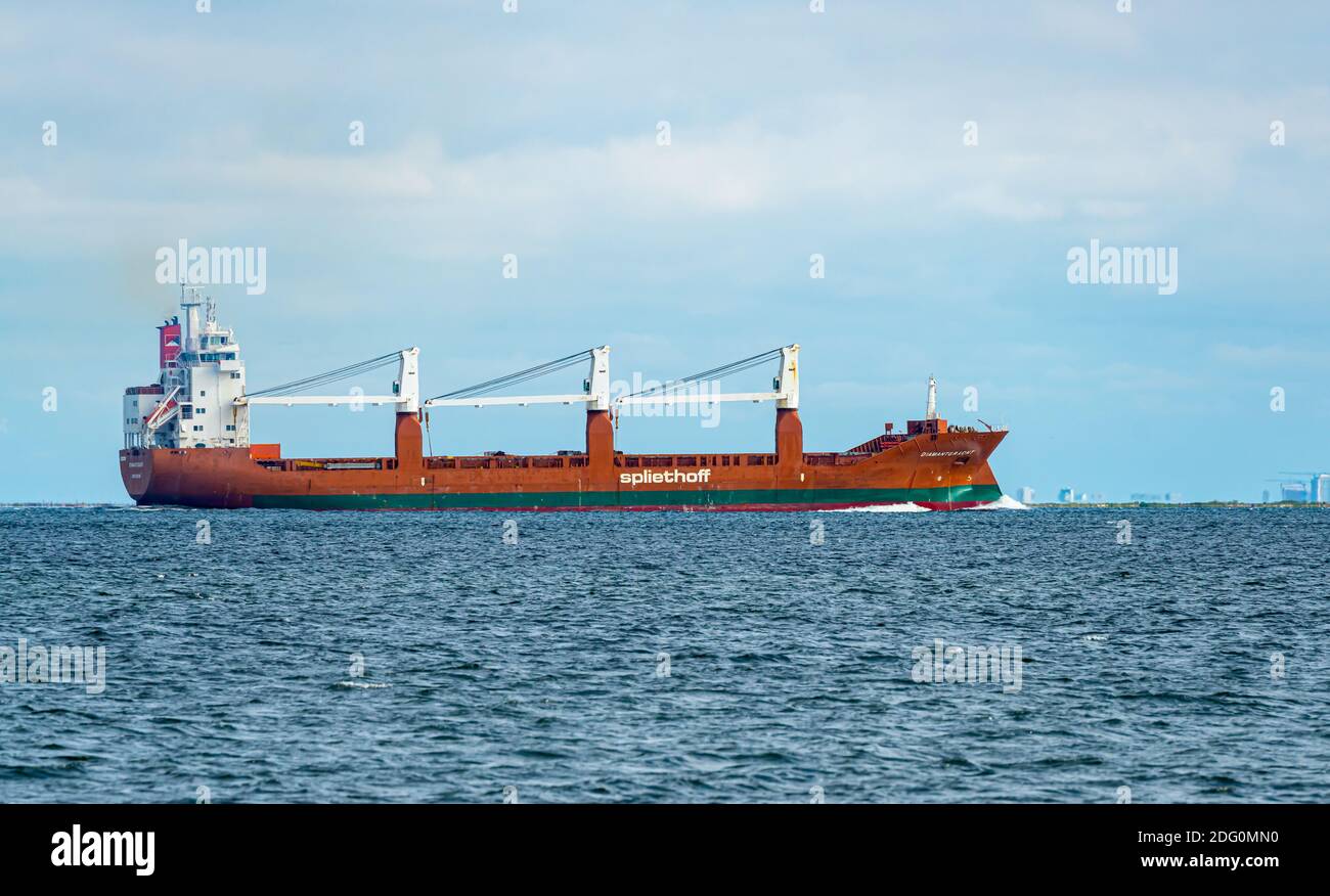 Red cargo ship with large cranes mounted onboard, sailing out to sea ...