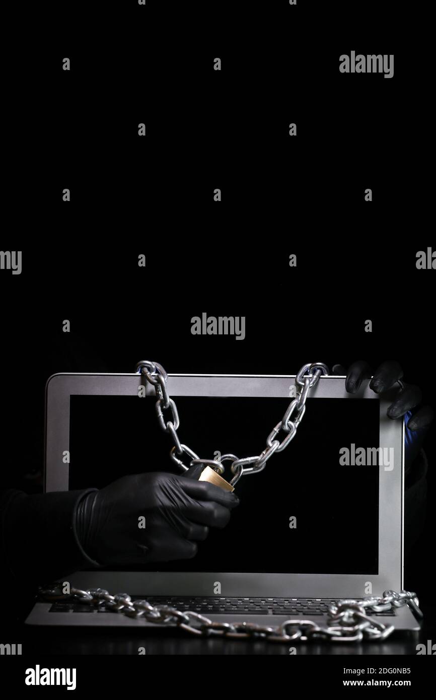 Laptop tied with an iron chain with a lock and hackers hands in a black ...