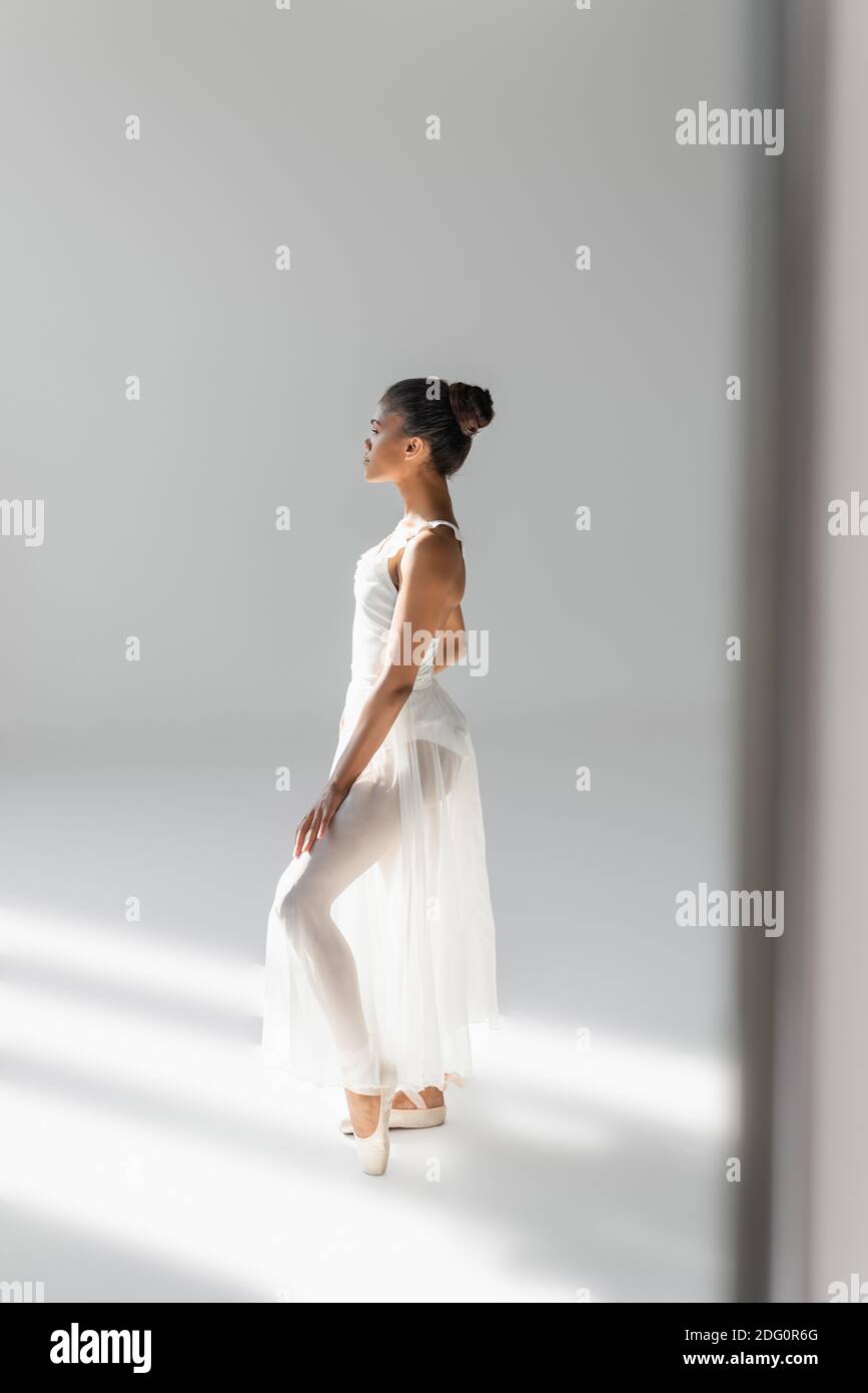 side view of graceful african american ballerina in dress on white ...