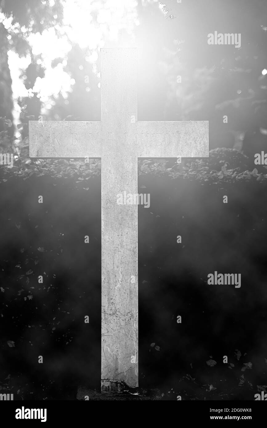Old stone cross tombstone in a graveyard with bright backlight and fog ...