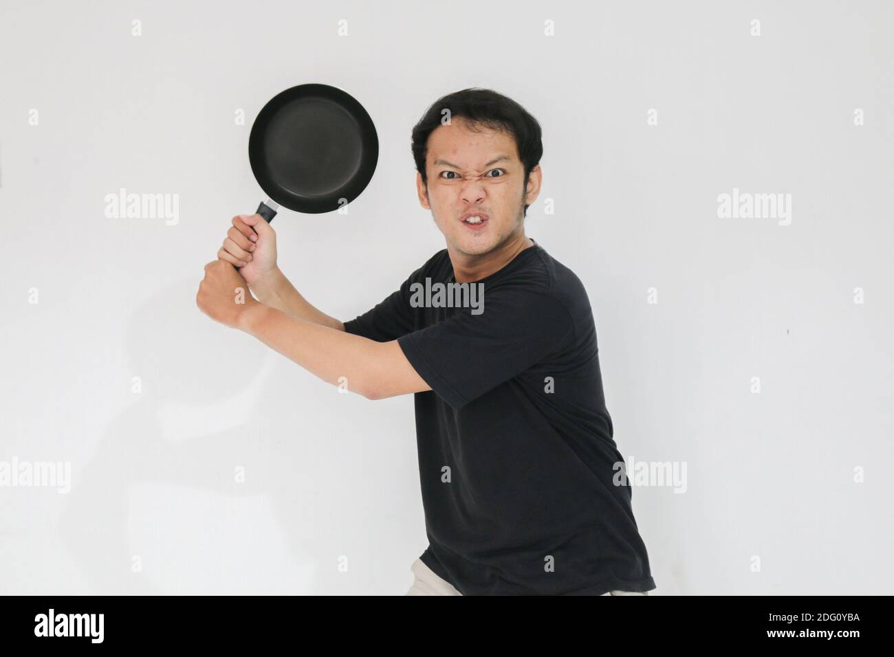 Young Asian man is angry and ready to strike with a frying pan ...