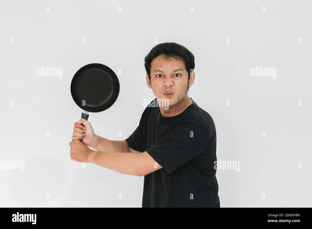 Young Asian man is angry and ready to strike with a frying pan ...