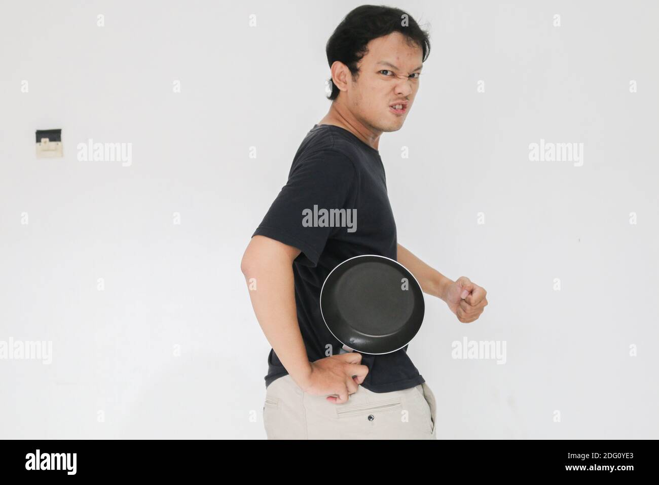 Young Asian man is angry and ready to strike with a frying pan ...