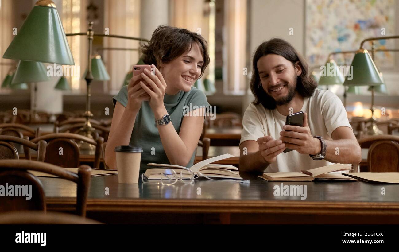 Attractive students happily using smartphones while preparing for exams ...