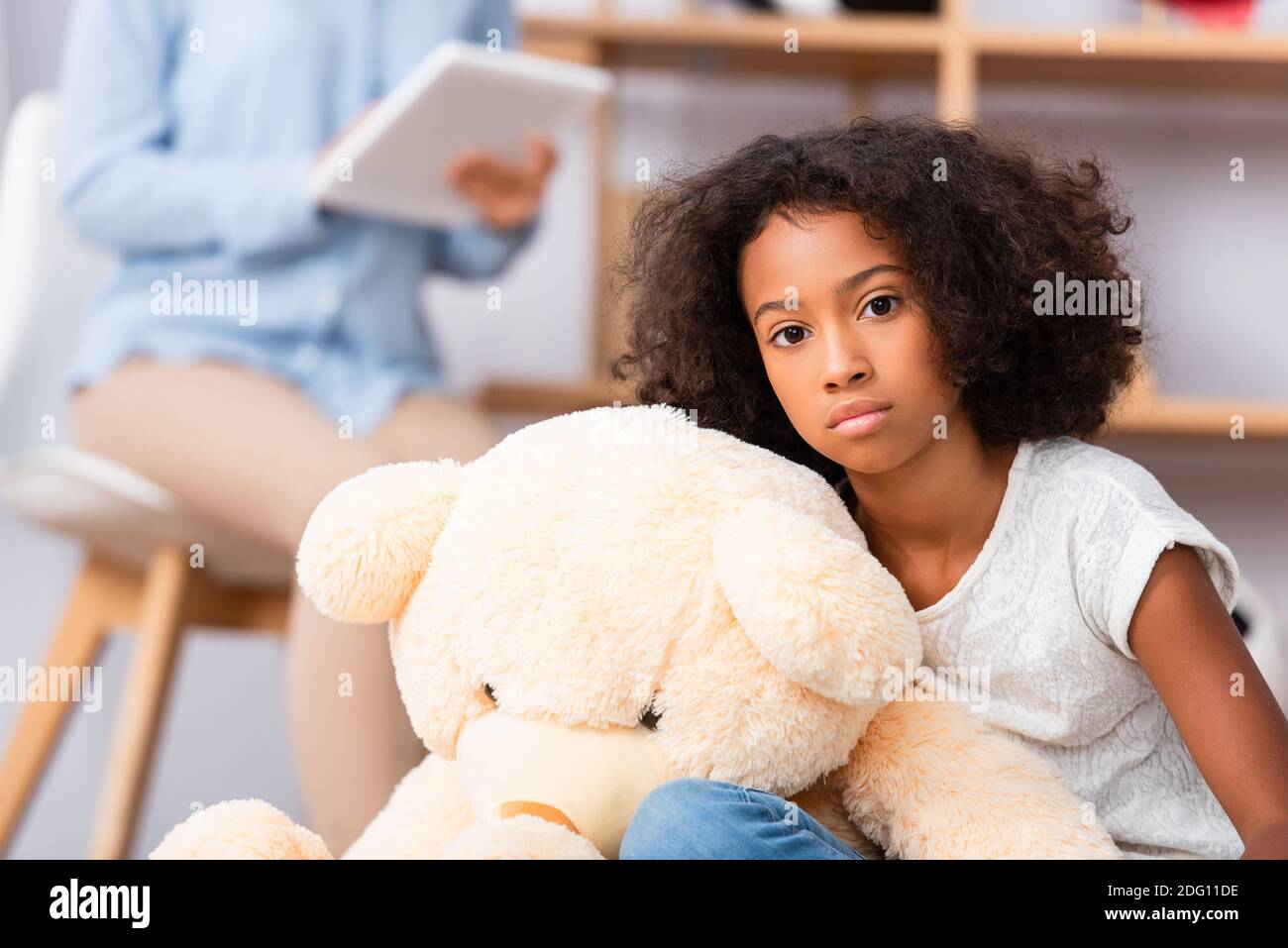 Lonely african american girl looking at camera near teddy bear with ...