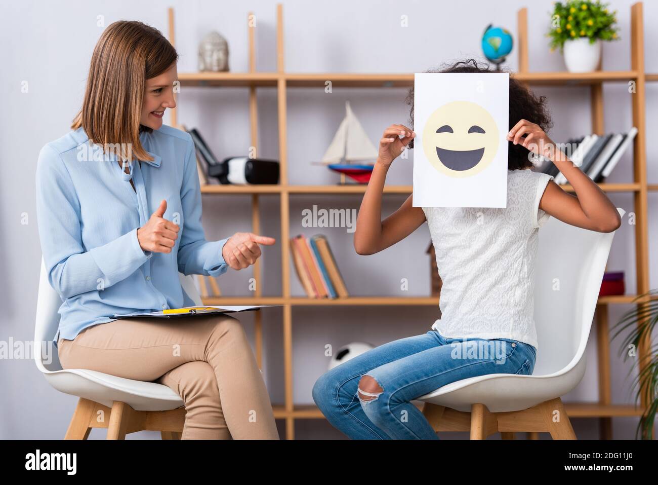 Smiling psychologist with thumbs up looking at african american girl ...
