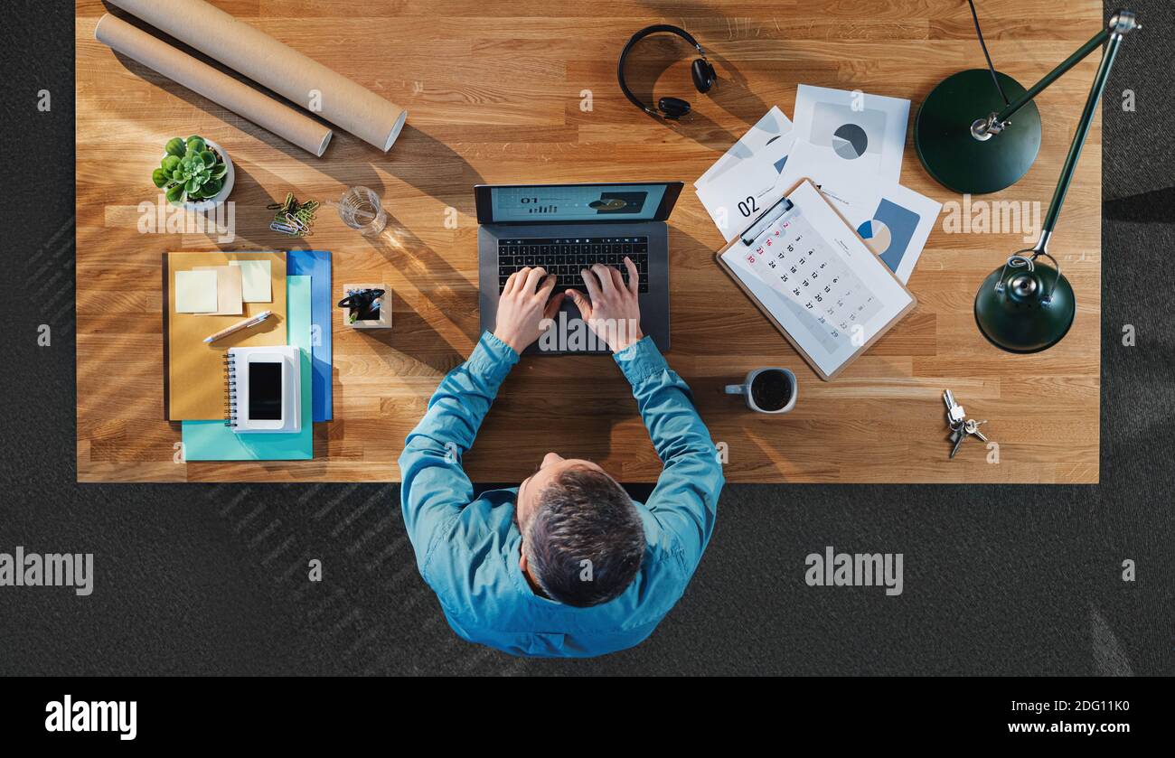 Top view of businessman working on computer at desk with paperwork in ...
