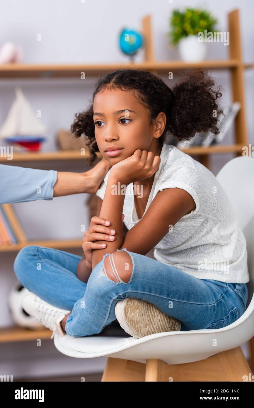 Upset african american girl with crossed legs sitting on chair with ...