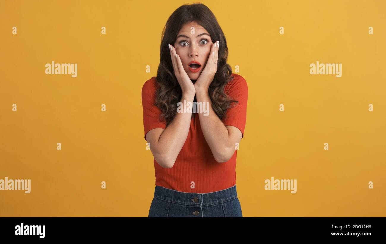 Attractive shocked girl in red top amazedly looking in camera isolated ...