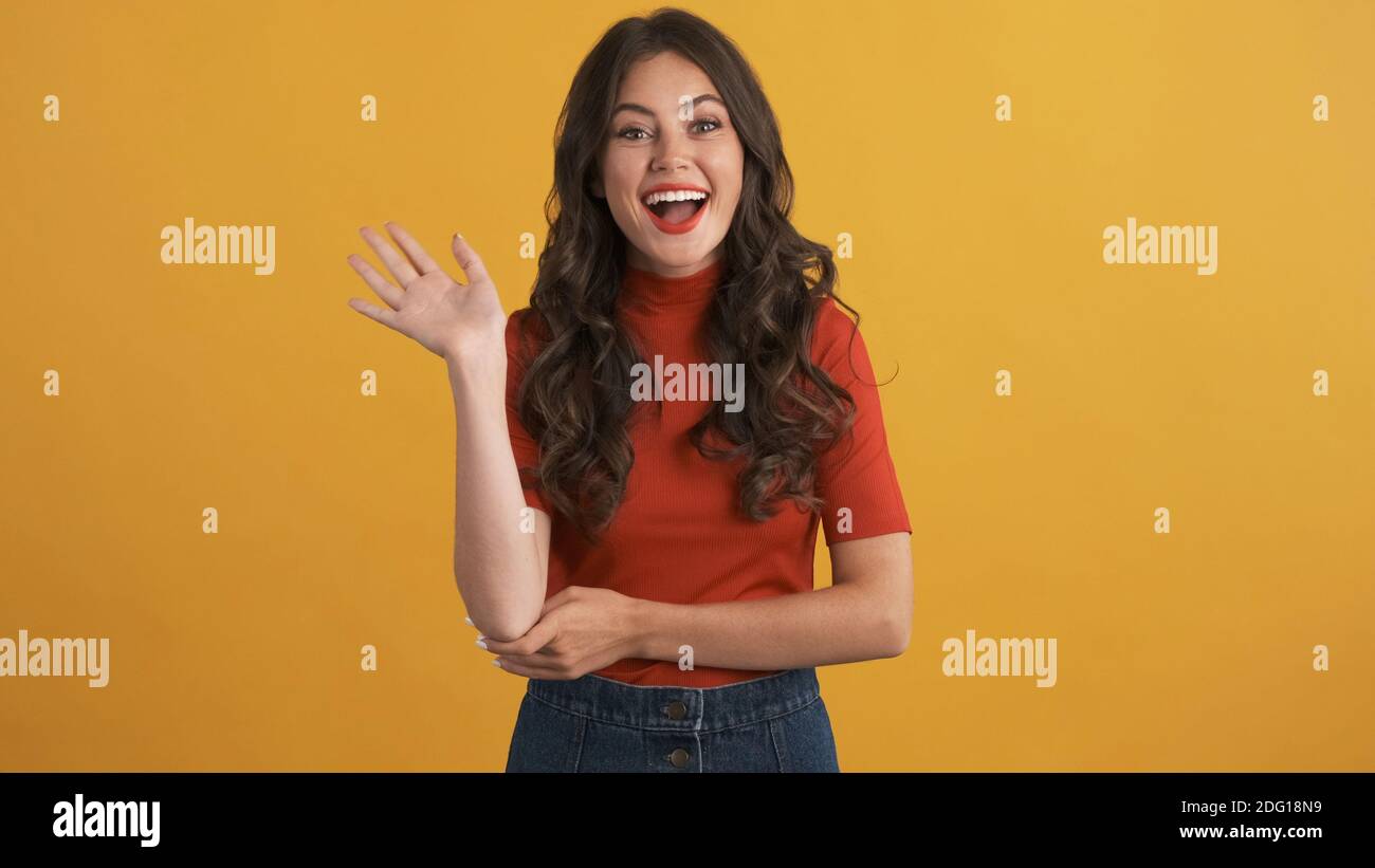 Pretty cheerful girl happily waving hello on camera over colorful ...