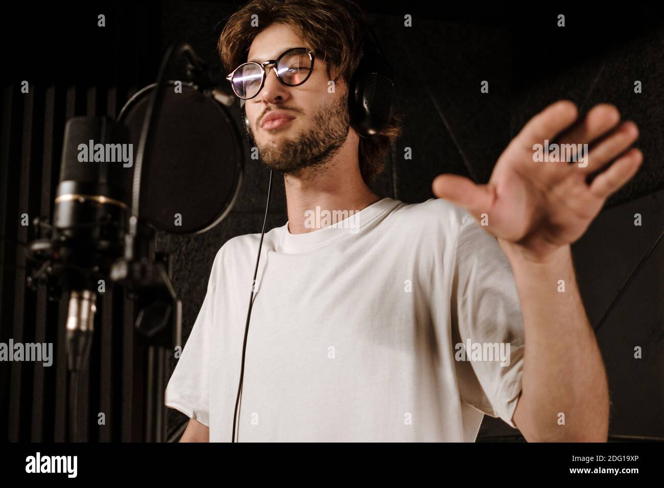 Portrait of young singer in headphones singing during record new song ...