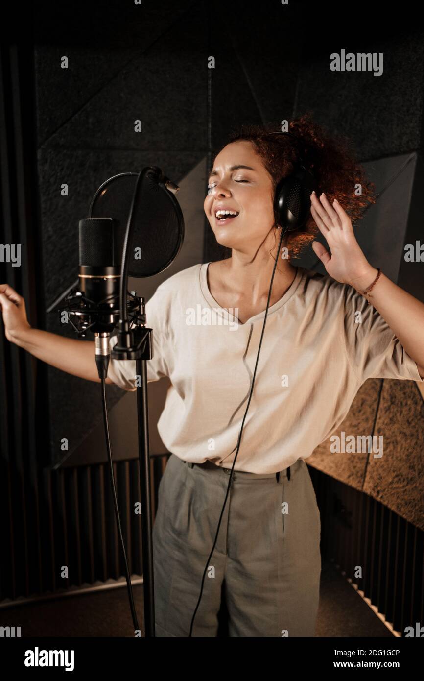 Attractive female musician in headphones emotionally singing in ...