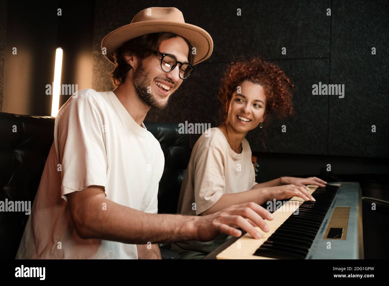 Young stylish musicians happily playing on piano keyboard recording ...