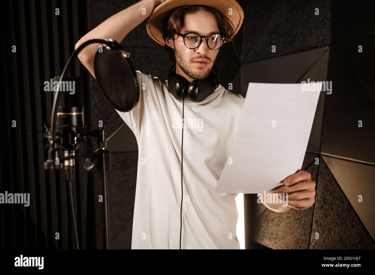 Young thoughtful male singer intently reading text of new song in sound ...