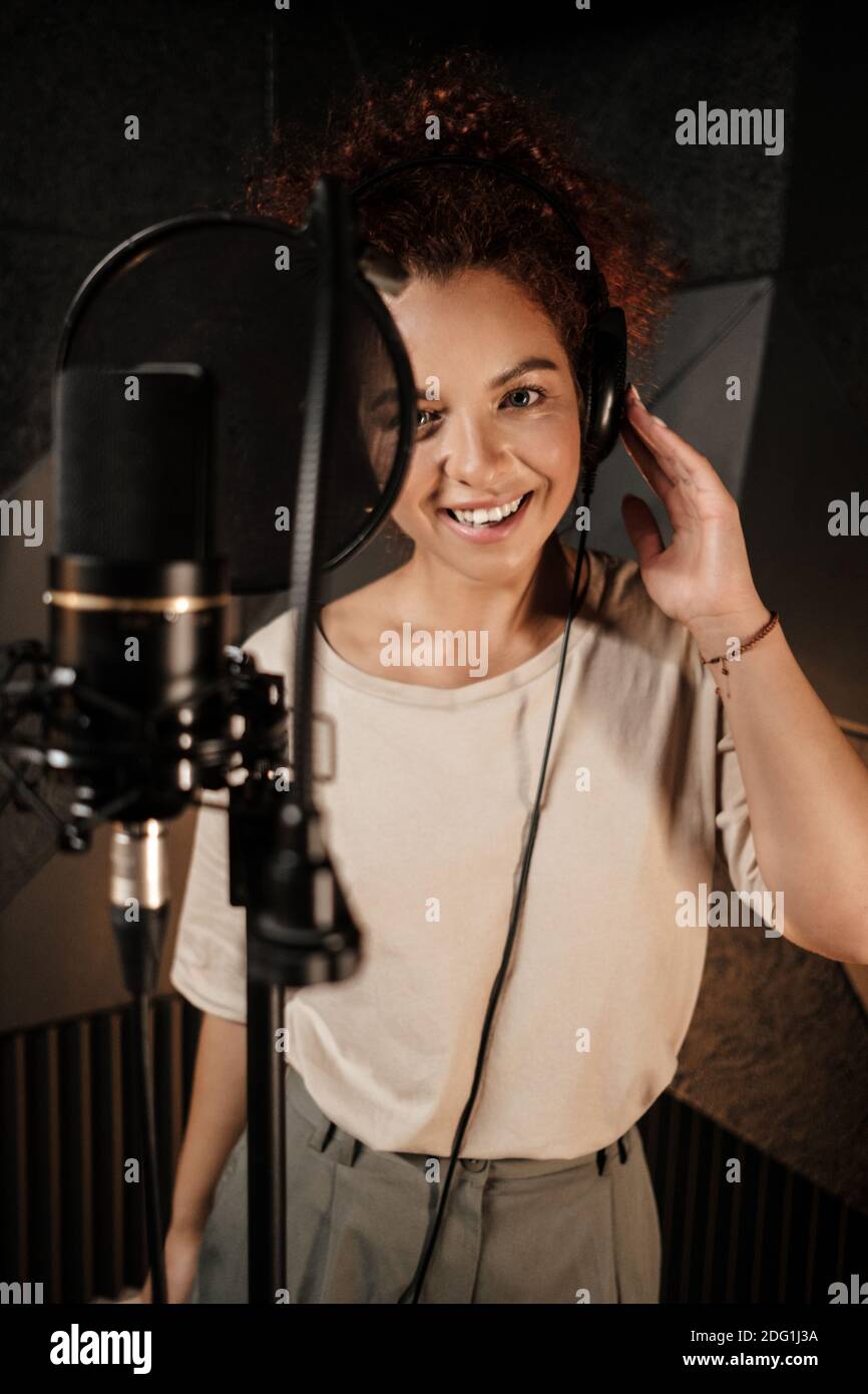 Pretty female singer in headphones happily looking in camera working on ...