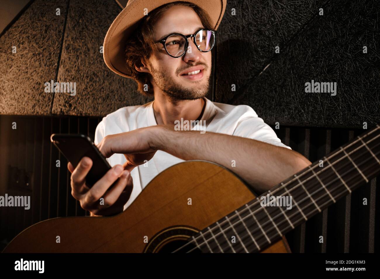 Portrait of attractive male musician with guitar and phone dreamily ...