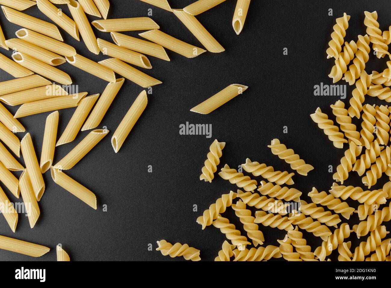 Raw pasta penne rigate and fusilli with copy space on black background ...