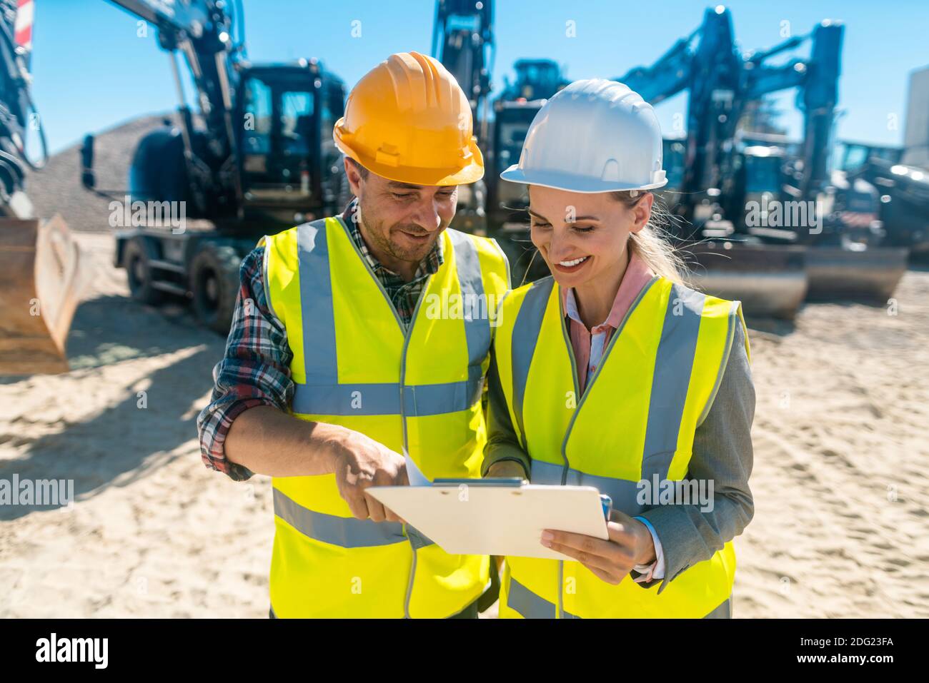 Two workers in open cast mine standing in front of heavy machinery ...