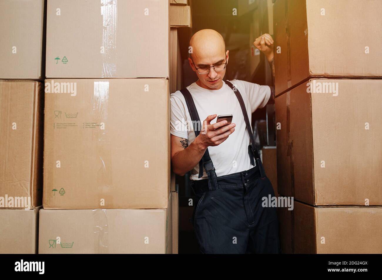 Tired bold man standing between high stacks of boxes, looking at his ...