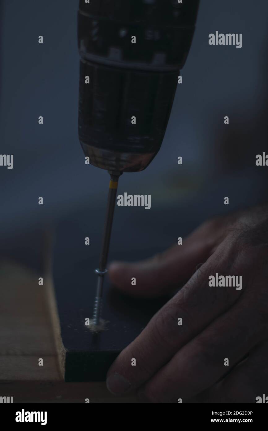 A vertical closeup of hands screwing a screw on a wooden board Stock ...
