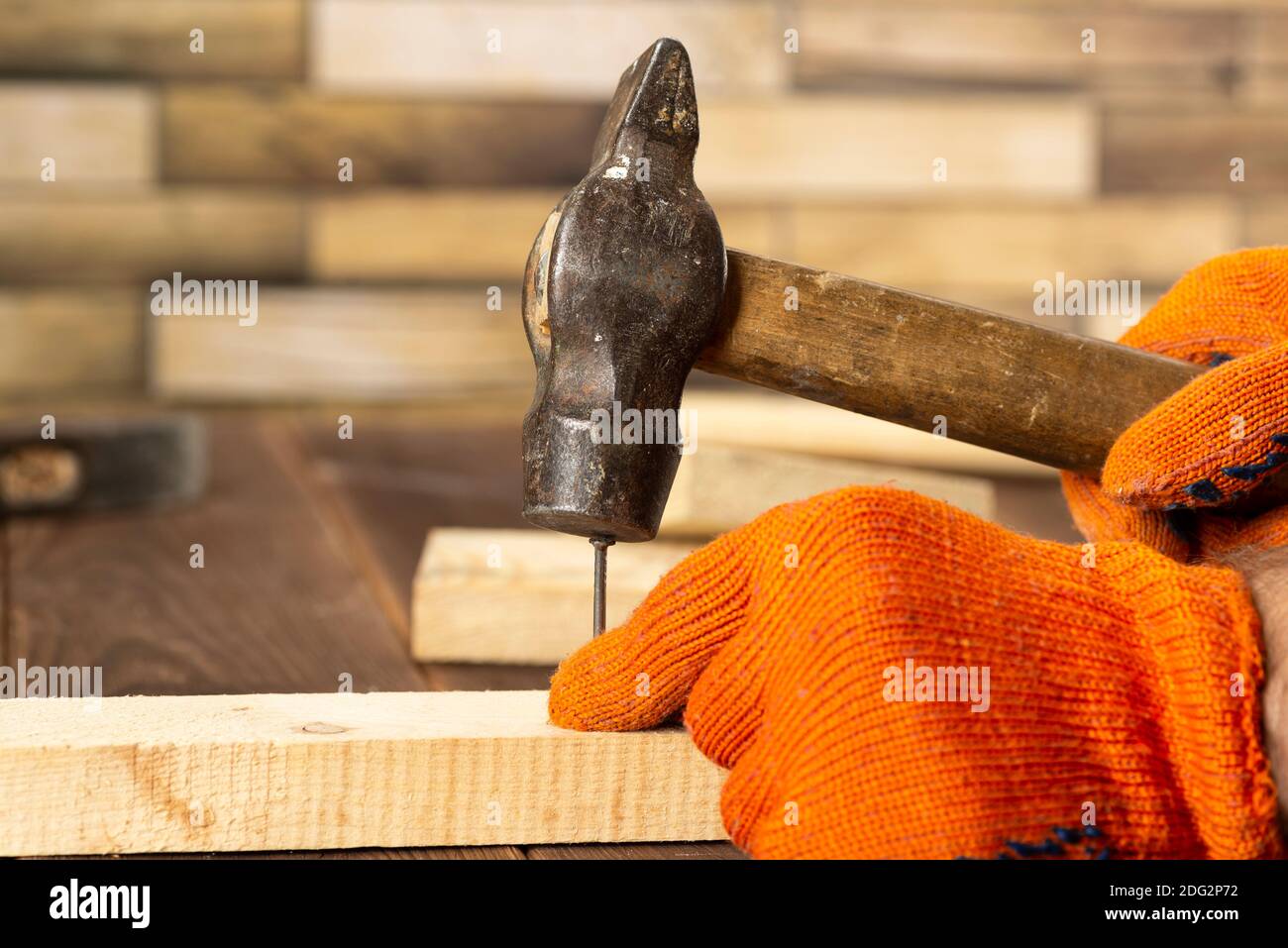 Close-up shot of a carpenter in orange work gloves hammers a nail into ...