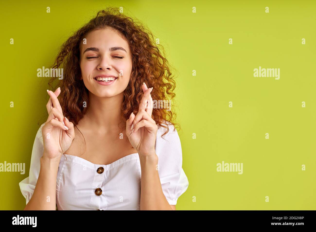 happy cute young woman with curly hair keeps fingers crossed, luck ...