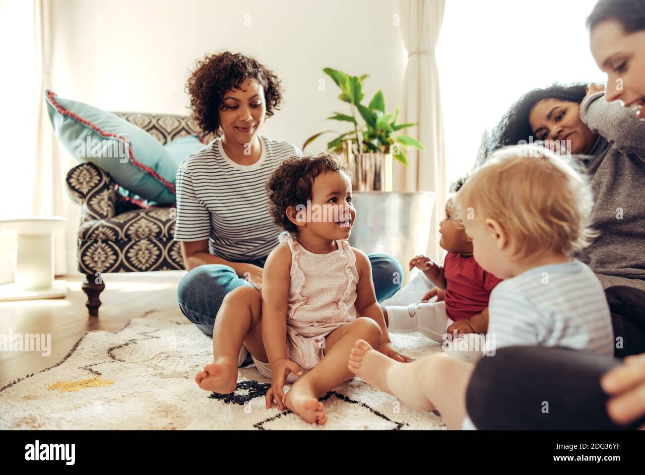 Mothers in the living room looking at their babies playing. Women ...