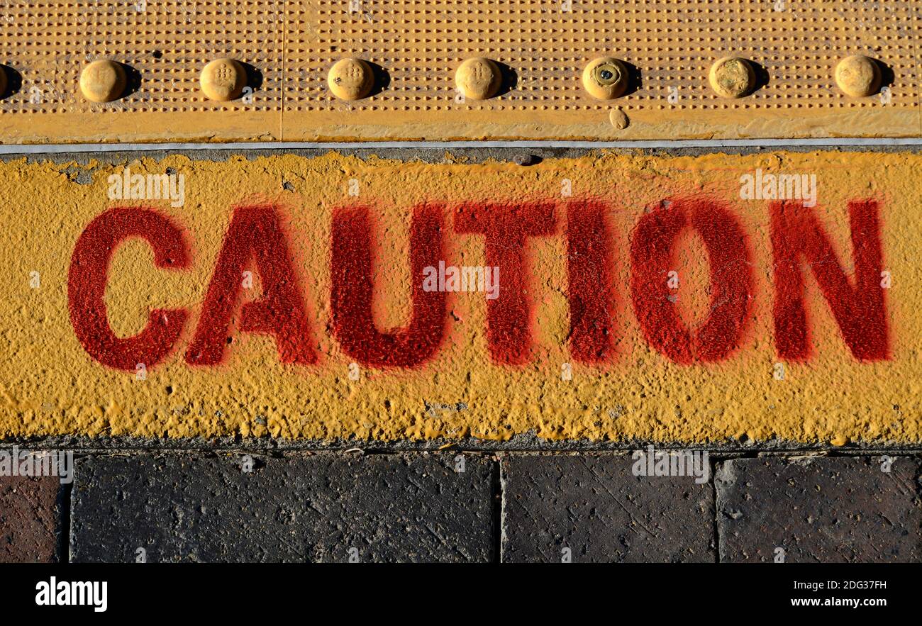 A yellow caution sign stenciled on a train station passenger platform ...