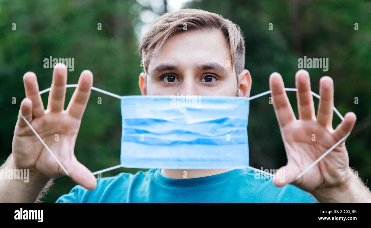 Scared Caucasian man holding blue medical mask in front of his face ...