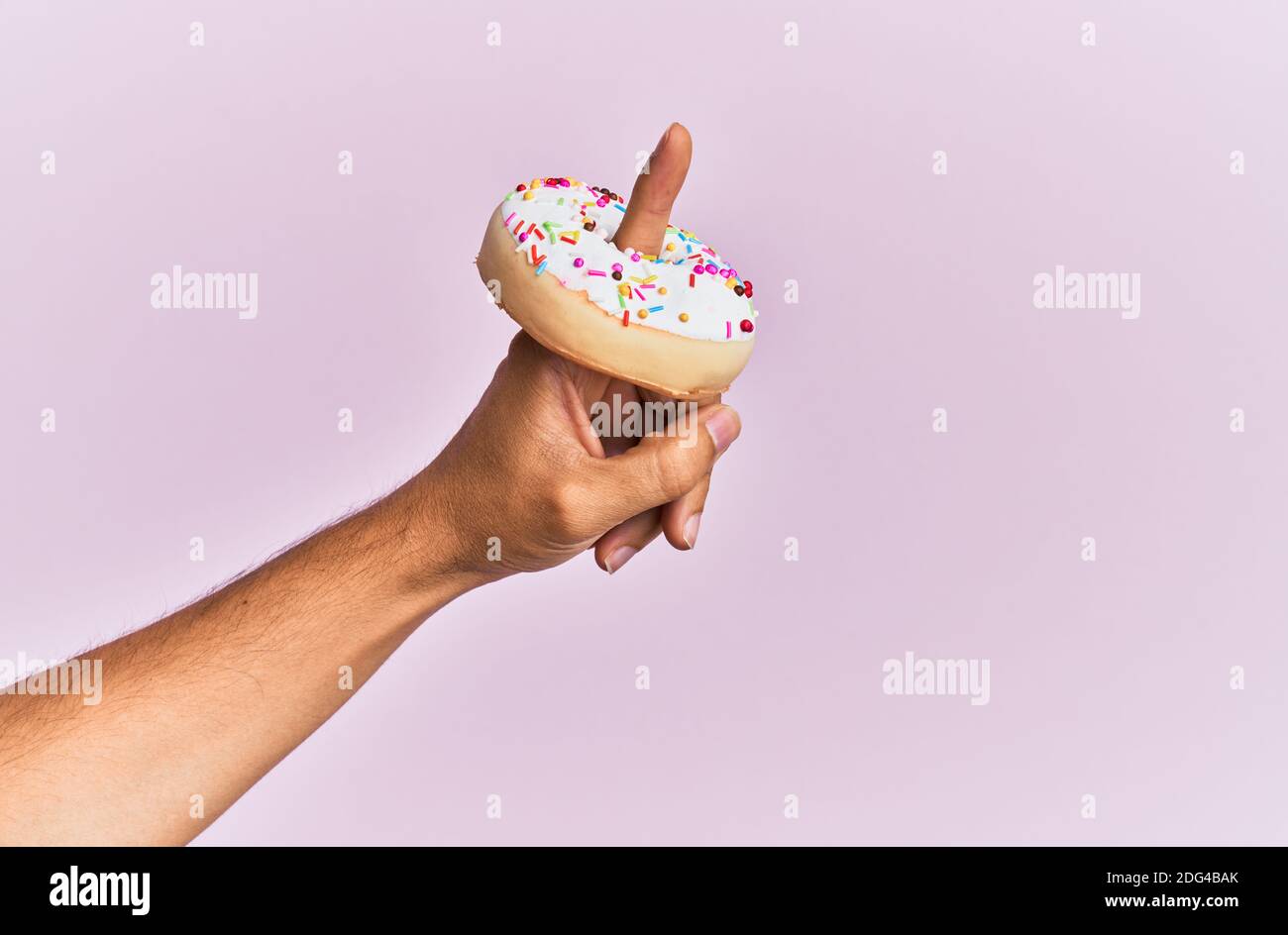 Finger of hispanic man holding donut over isolated pink background ...