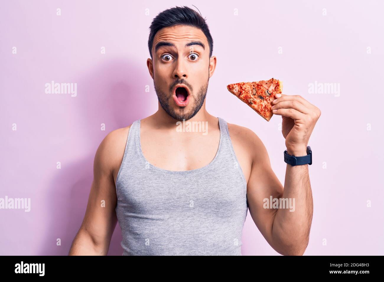 Young handsome man with beard eating slice of Italian pizza over ...