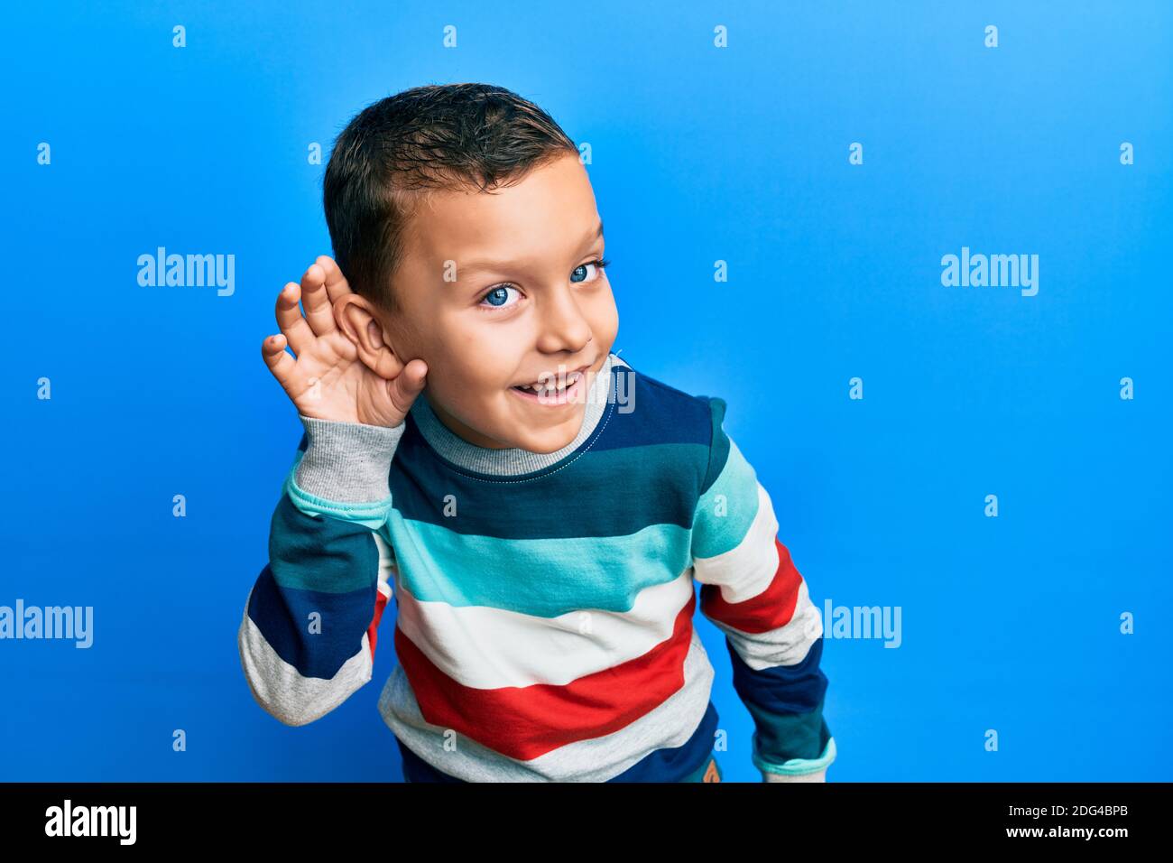 Little kid boy wearing striped sweater smiling with hand over ear ...
