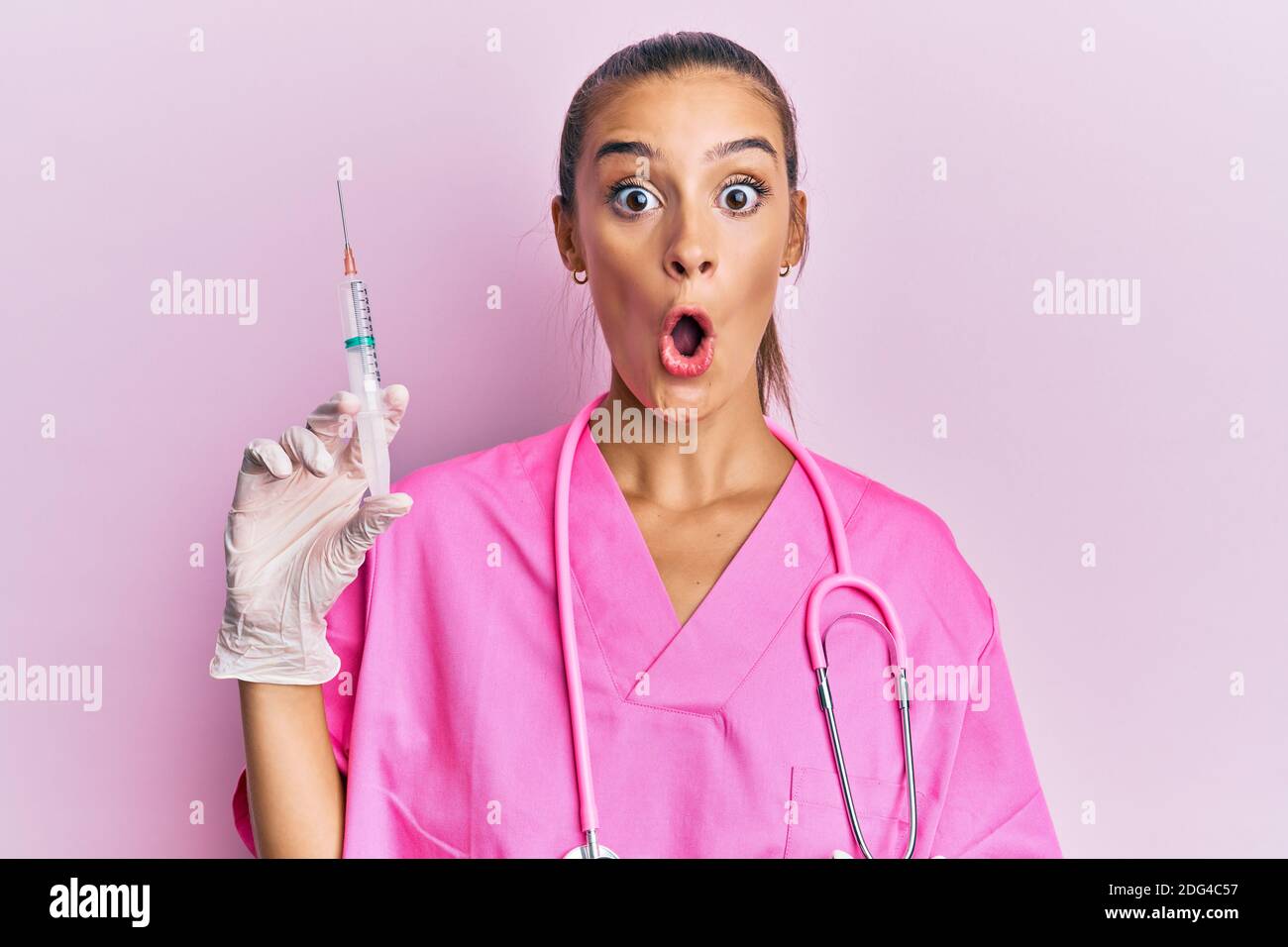 Young hispanic woman wearing doctor stethoscope holding syringe scared ...