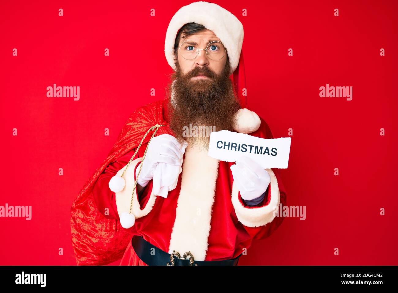Handsome young red head man with long beard wearing santa claus costume ...
