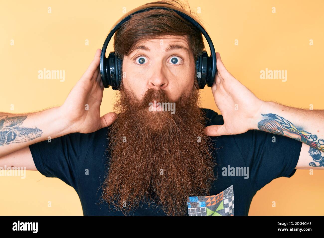Handsome young red head man with long beard listening to music using ...