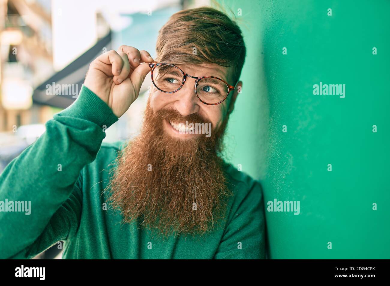 Young irish man with redhead beard smiling happy leaning on the wall at ...
