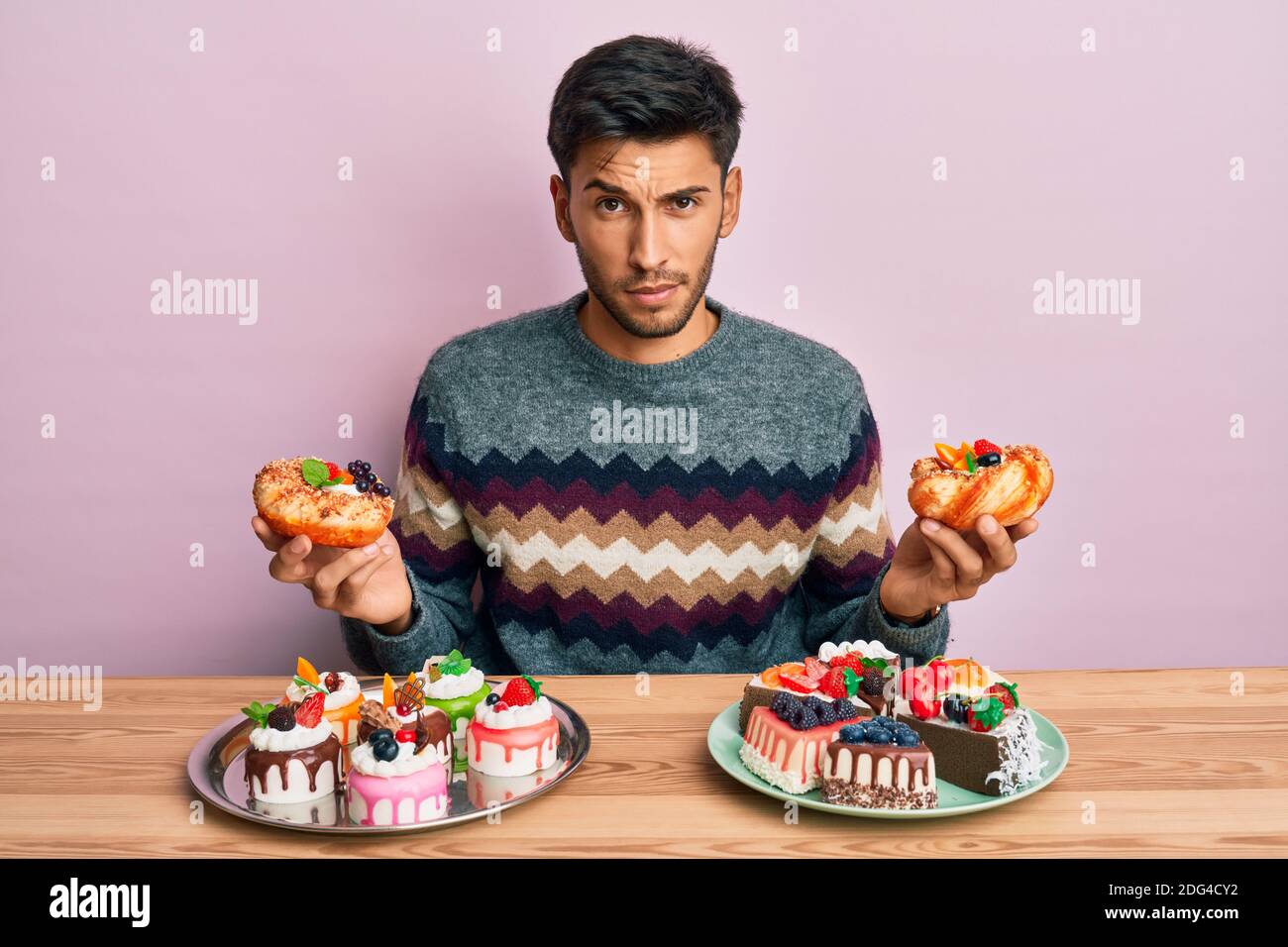 Young handsome man holding sweet pastries skeptic and nervous, frowning ...