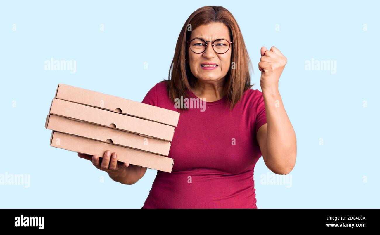Middle age latin woman holding delivery pizza box annoyed and ...